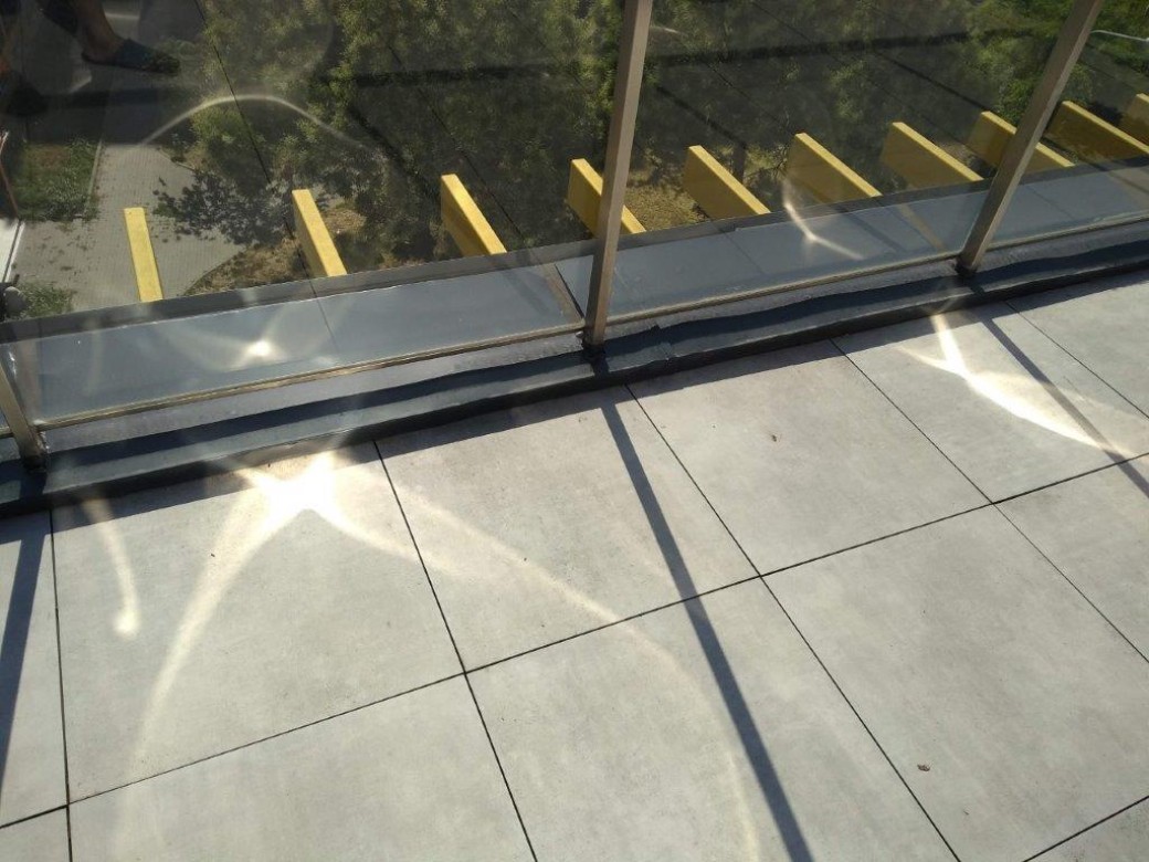 Poškození PVC fólie kolem skleněného zábradlí na terase bytového domu